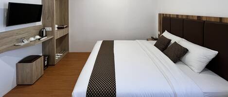 Quarto de hotel moderno com uma cama grande, televisão fixada na parede, guarda-roupa de madeira e mesa de cabeceira com abajur.