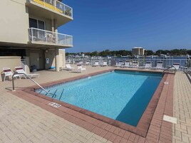 Piscina retangular com indicador de profundidade de 90 centímetros, rodeada por espreguiçadeiras e um edifício com varanda.