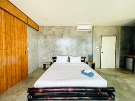 Quarto de hotel com uma cama grande, painéis de madeira em uma parede, parede com textura de mármore, uma porta branca e uma pequena escrivaninha com abajur.