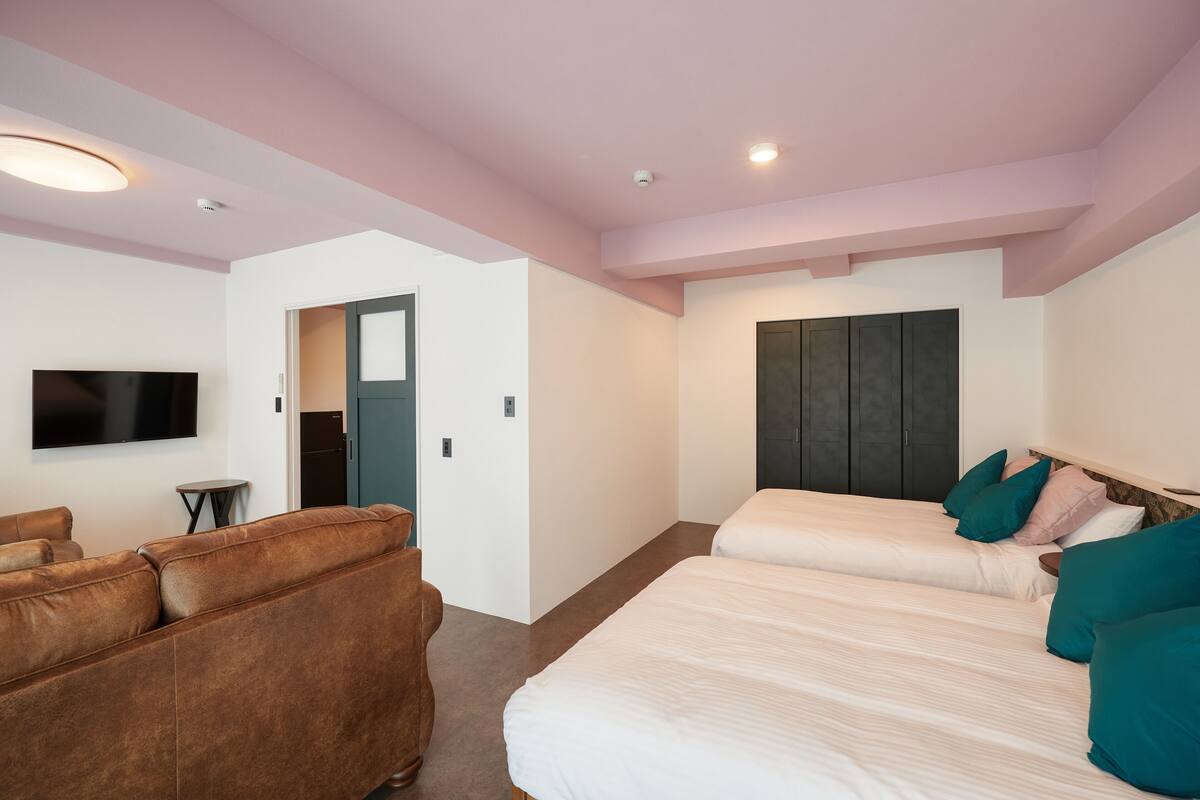 Quarto de hotel moderno com uma cama grande, um sofá, uma TV de tela plana e um guarda-roupa.