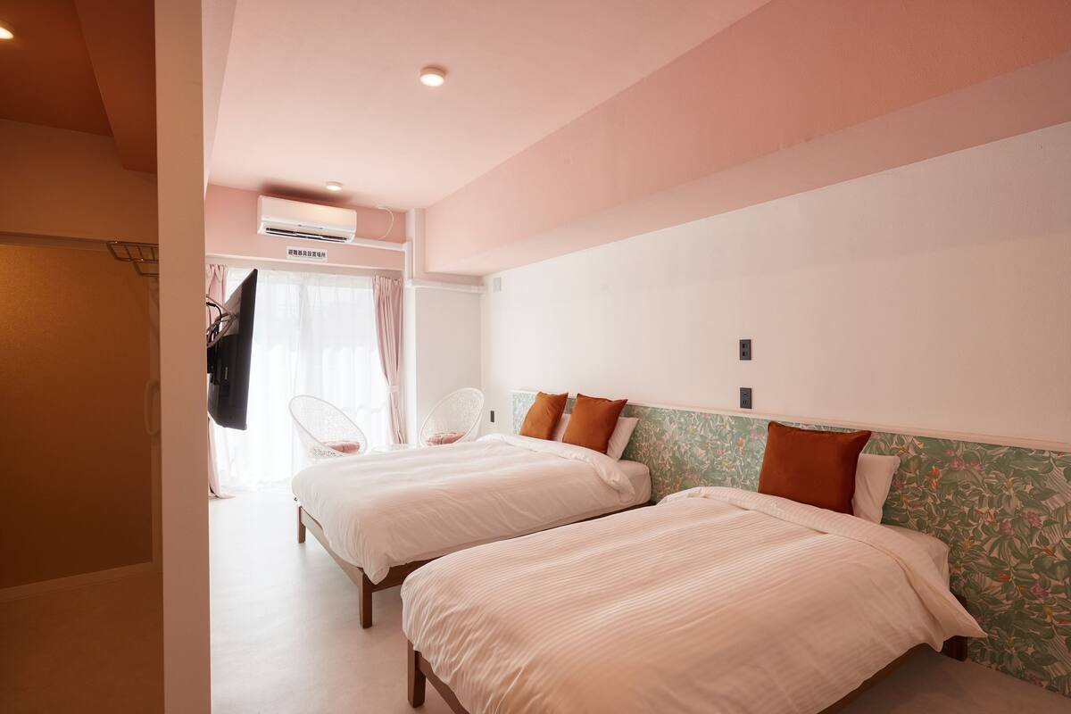 Quarto de hotel com duas camas, televisão e janela com cortinas.