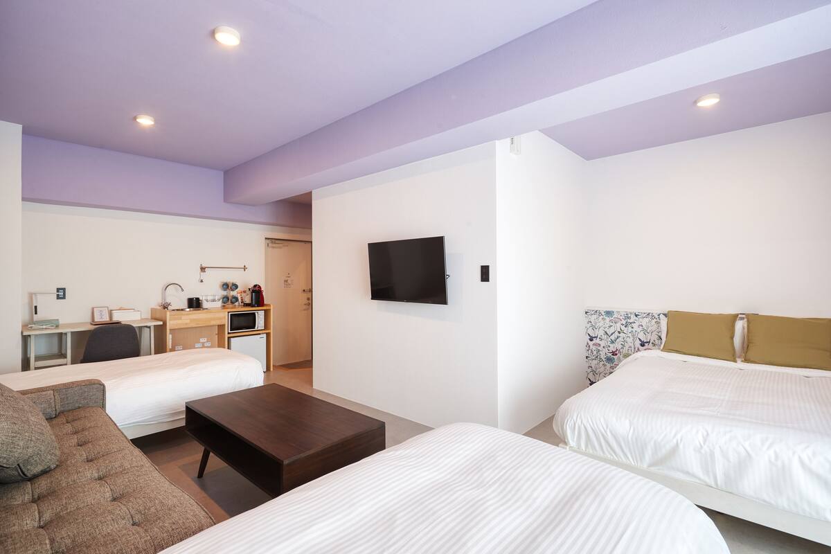 Quarto de hotel moderno com duas camas, um sofá, uma escrivaninha, uma televisão de tela plana e um micro-ondas.