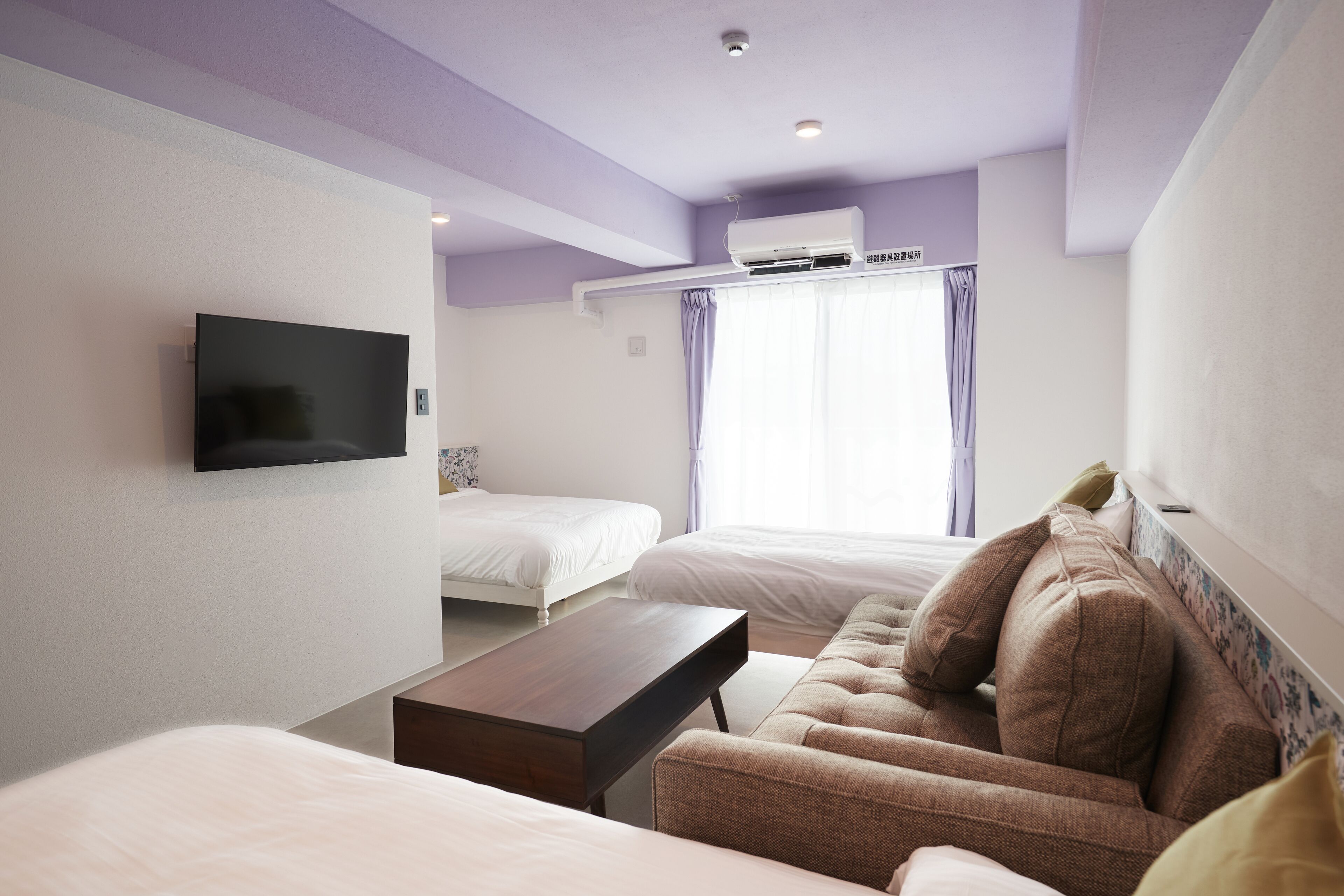 Quarto de hotel com duas camas, um sofá, uma televisão e um aparelho de ar condicionado.