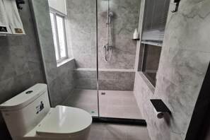 Um banheiro com vaso sanitário, chuveiro com porta de vidro e janela.