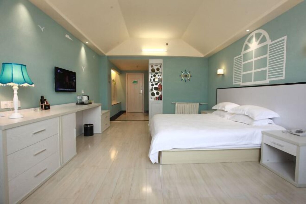 Quarto com cama, mesas de cabeceira, escrivaninha, luminária, radiador e televisão.