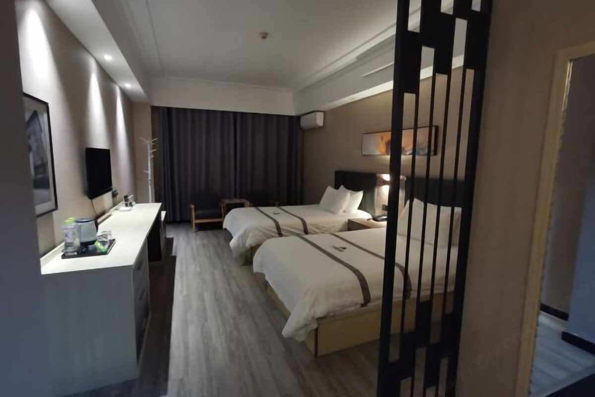 Quarto de hotel com duas camas, uma mesa, uma cadeira e uma televisão.