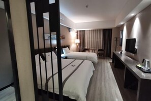 Quarto de hotel com duas camas, uma escrivaninha, uma cadeira, uma televisão e uma janela com cortinas.