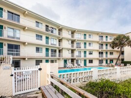 Um hotel com vários andares, piscina, área de estar externa e entrada com portão.