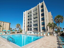 Um hotel com área de piscina, várias varandas e palmeiras.