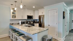 Uma cozinha moderna com armários brancos, eletrodomésticos de aço inoxidável, uma ilha de mármore com banquetas e iluminação pendente.