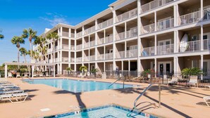 Um hotel com ampla área de piscina, várias varandas e palmeiras.