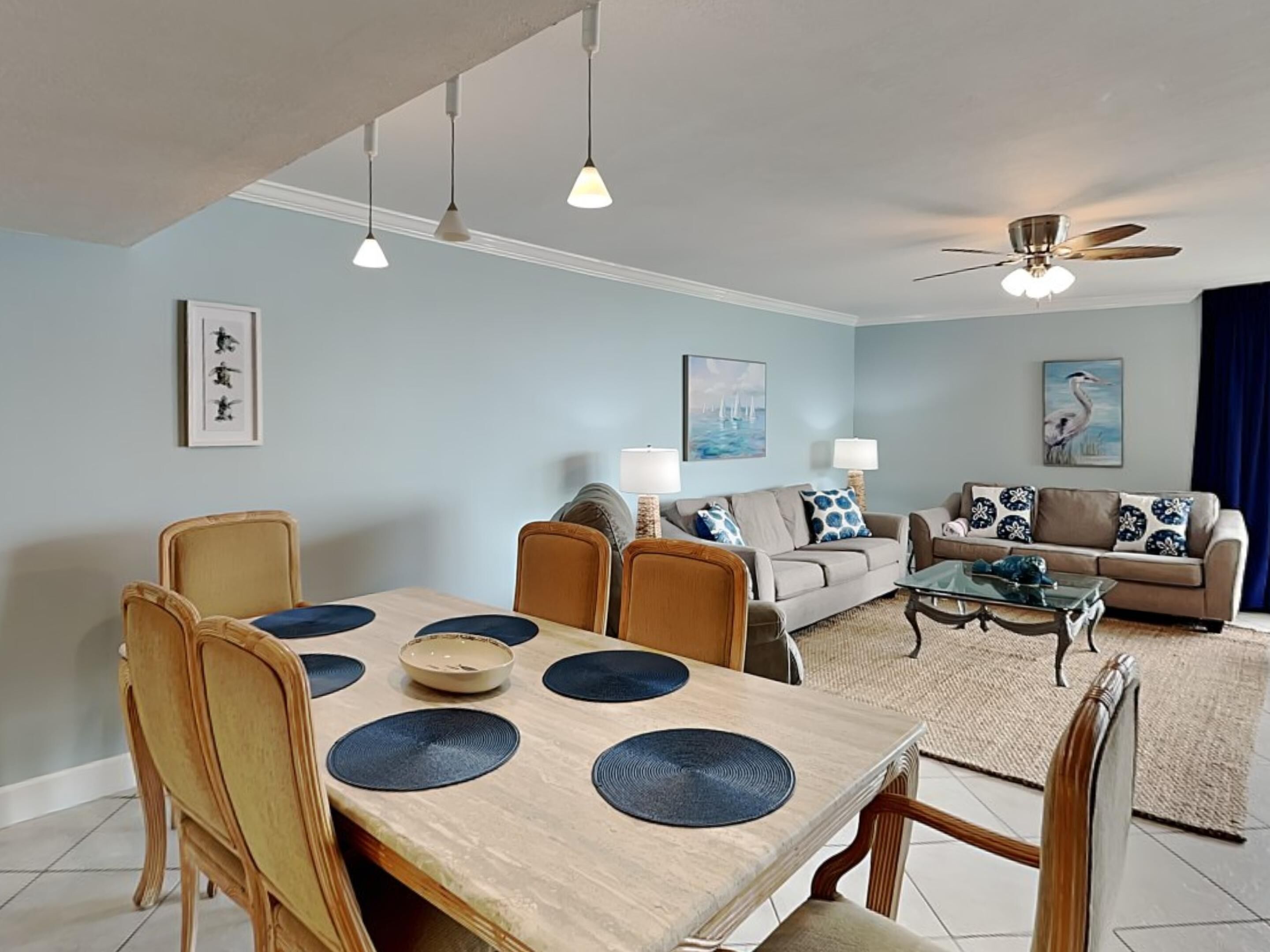 Uma sala de estar com mesa de jantar, cadeiras, sofás e um ventilador de teto.
