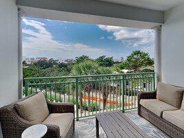 Varanda com móveis de vime e vista para uma paisagem verde e edifícios.