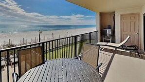 Uma varanda com vista para a praia, uma porta e uma pequena mesa com cadeiras.