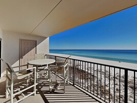 Uma varanda com mesa e cadeiras, uma porta e vista para a praia.
