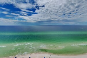 Uma praia com águas turquesa cristalinas, areal arenoso e céu parcialmente nublado.