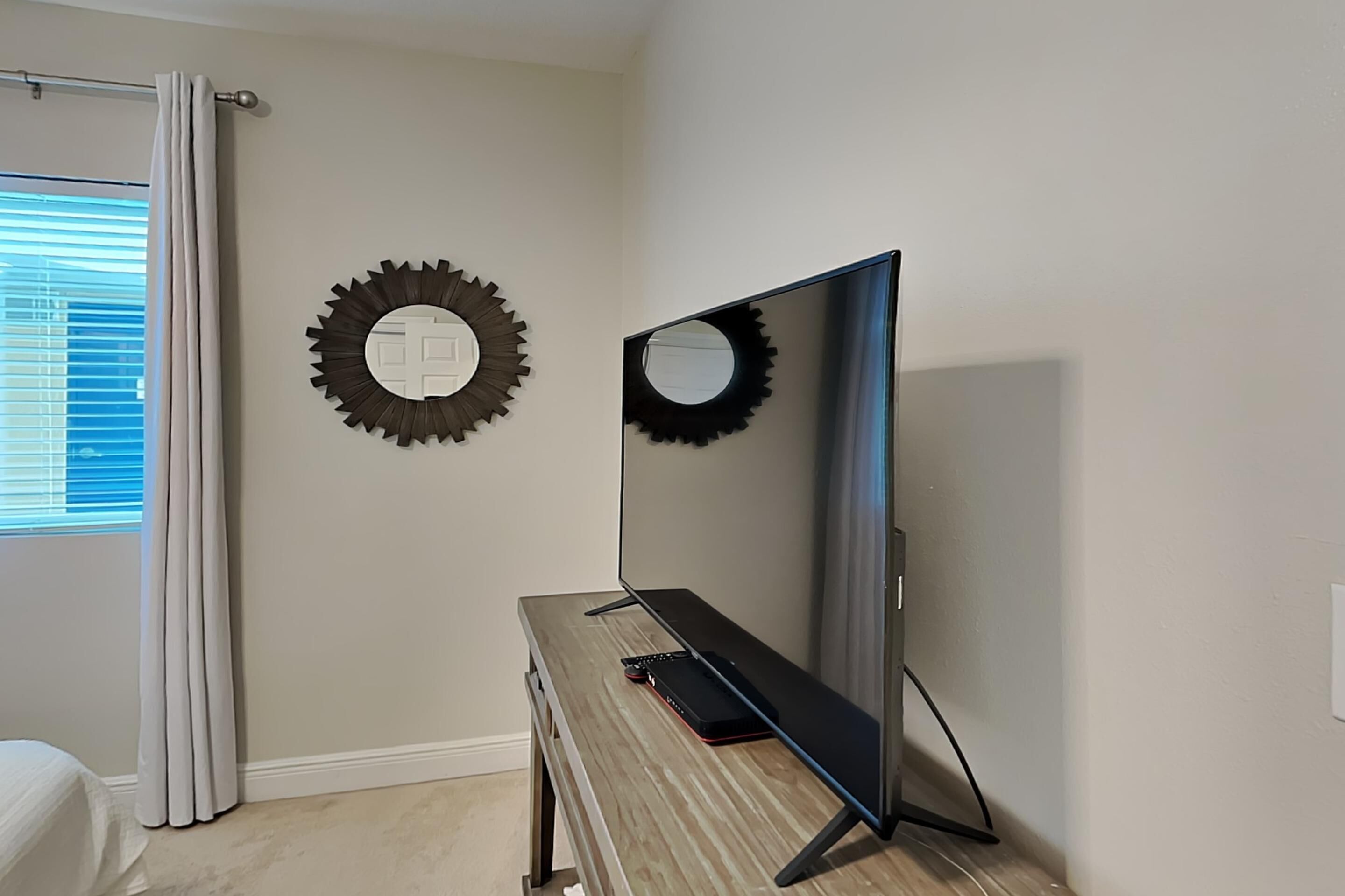 Quarto com televisão sobre suporte de madeira, espelho e peça decorativa de engrenagens na parede.