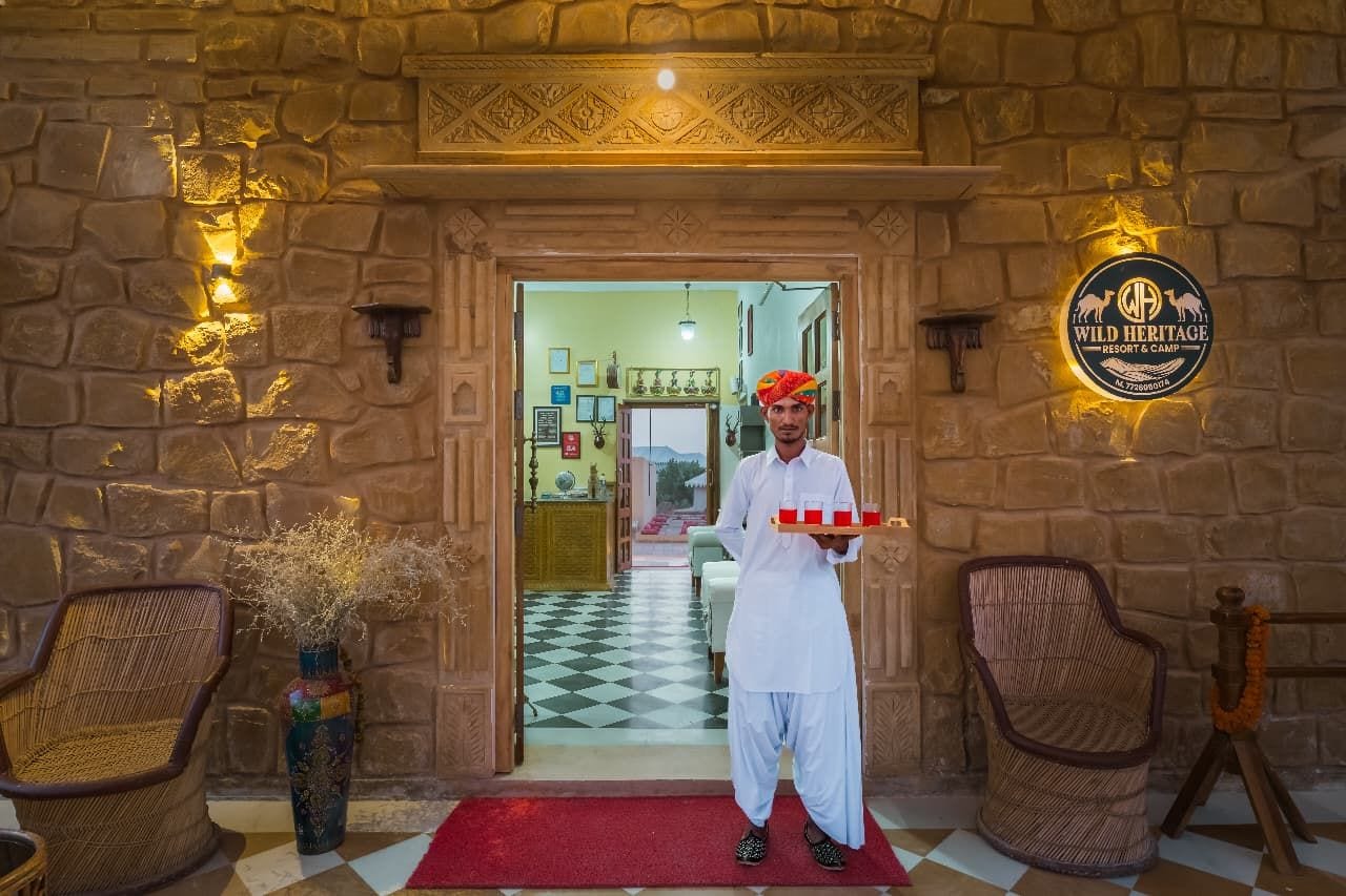 Um homem está em frente à entrada de um edifício com uma placa que diz 'Wild Heritage Resort & Camp'.