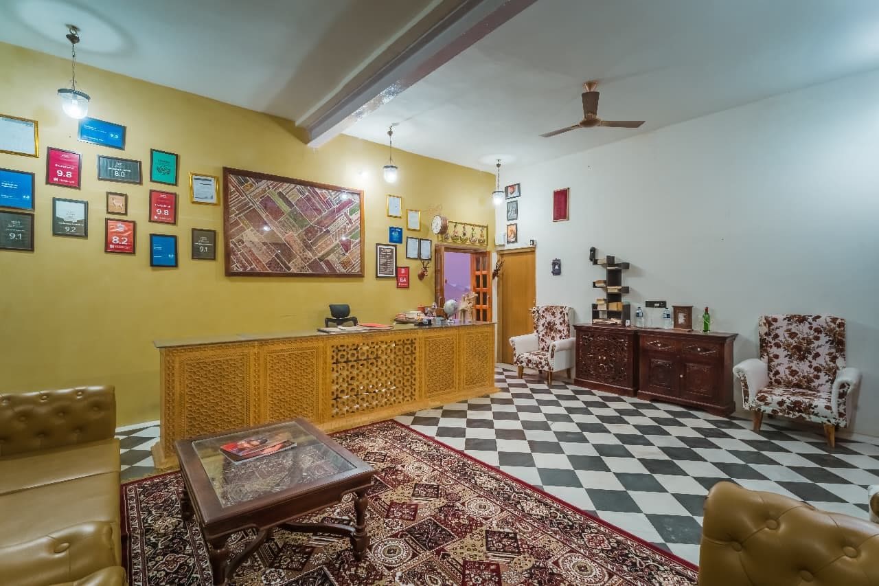Um saguão de hotel com piso xadrez, balcão de recepção e área de estar com tapete estampado.
