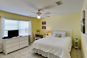 Quarto com cama, escrivaninha, televisão e ventoinha no teto.