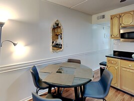 Uma cozinha compacta com área de refeições, apresentando uma mesa redonda com cadeiras, armários de madeira e micro-ondas embutido.