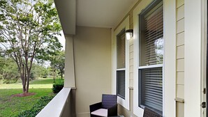 Varanda com móveis de vime e vista para um gramado verde e árvores.