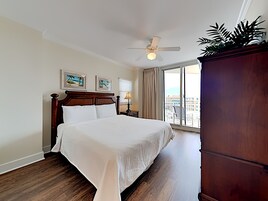 Quarto de hotel com uma cama grande, um ventilador de teto, uma mesa de cabeceira com abajur e vista para a cidade pela janela.