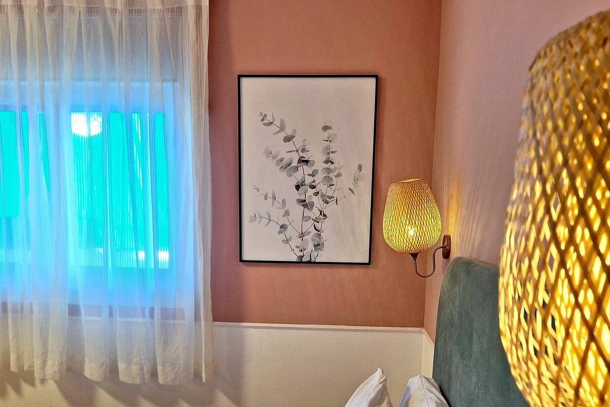 Uma cama bem arrumada com lençóis brancos, uma impressão botânica emoldurada na parede e uma luminária de parede com textura.