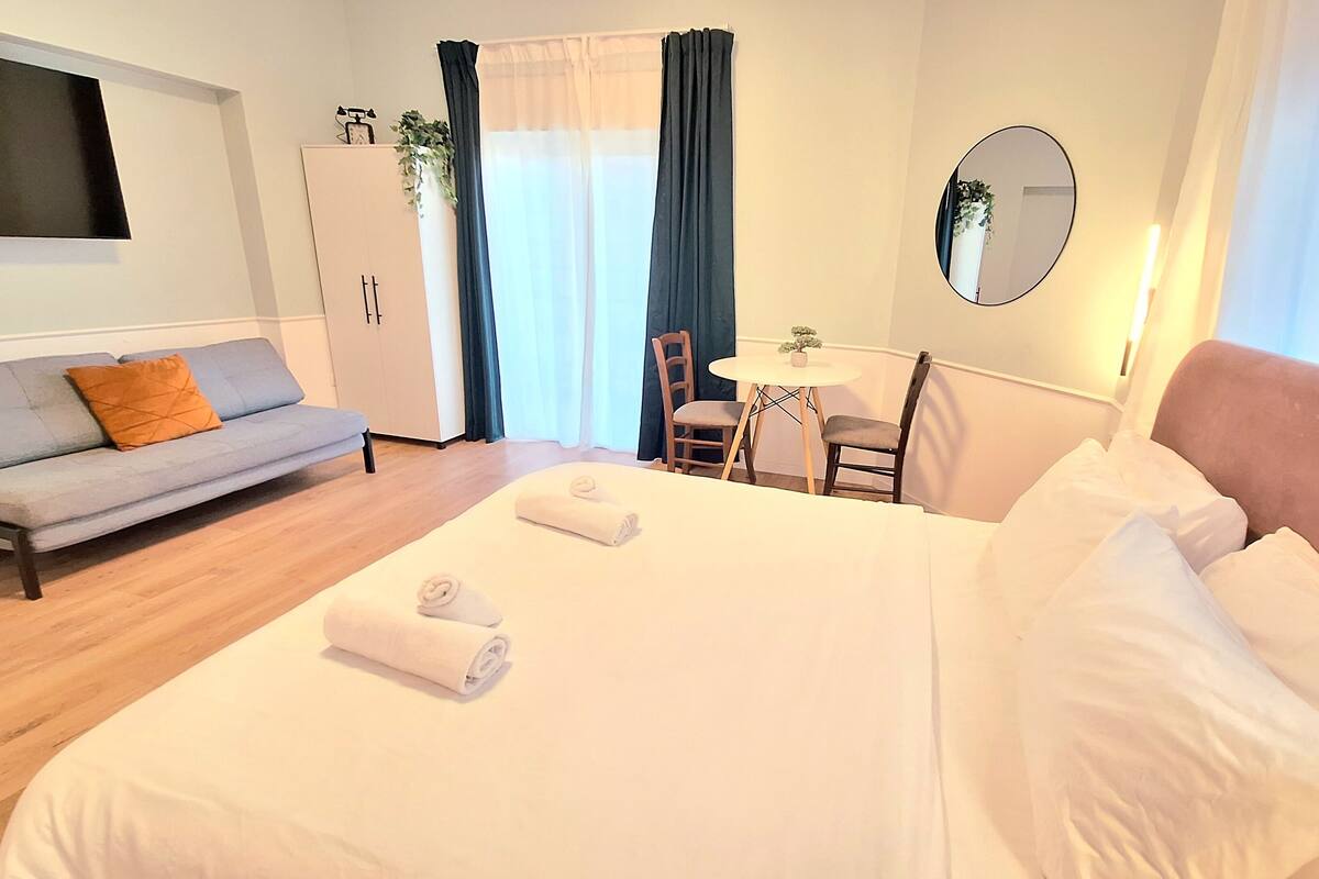 Quarto de hotel com uma cama grande, um sofá, uma escrivaninha e um espelho.