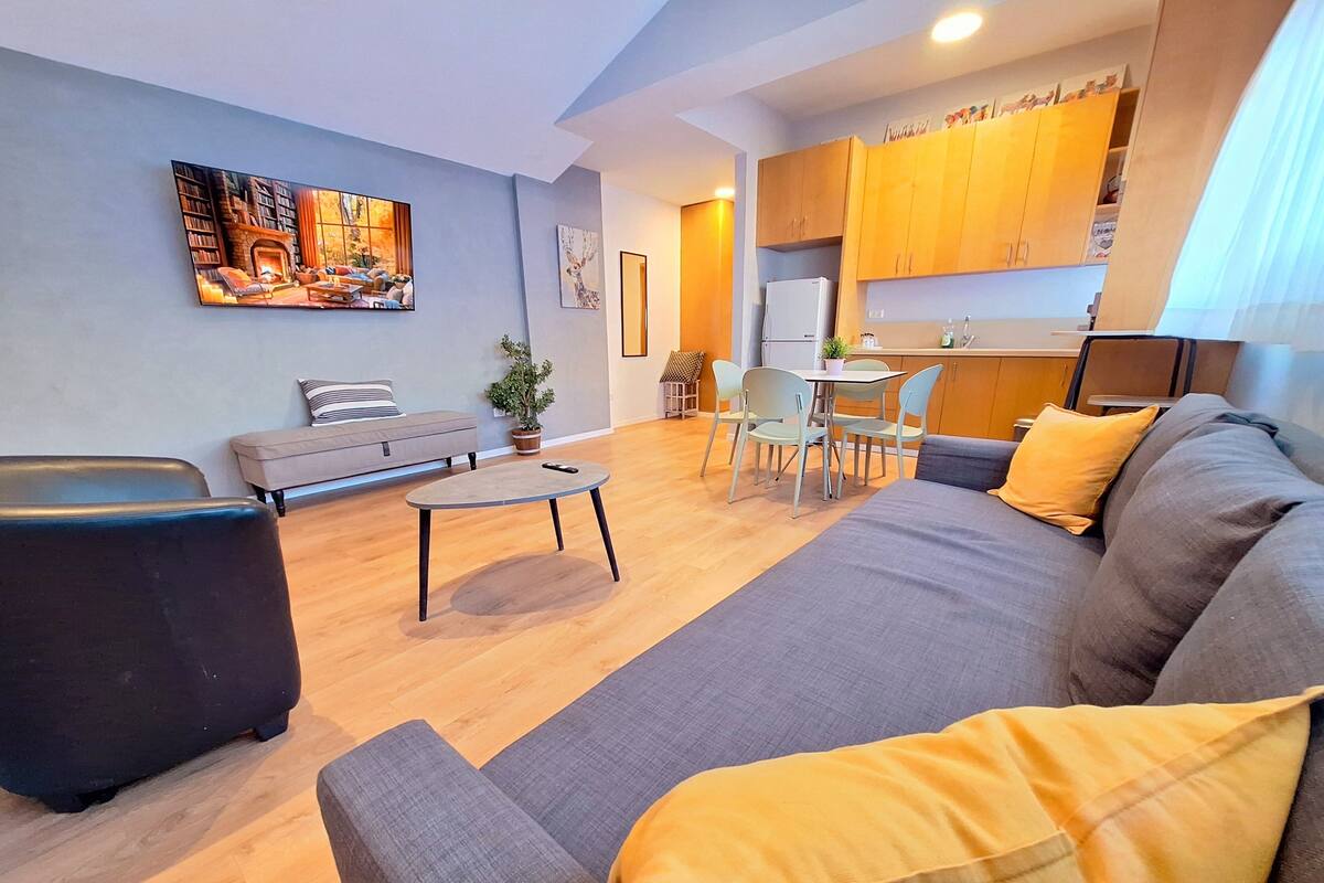 Uma sala de estar moderna com um sofá, uma mesa de centro e um espaço de jantar com cadeiras e uma pequena mesa.
