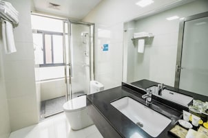 Uma casa de banho moderna com cabine de chuveiro em vidro, bancada preta e um espelho grande.