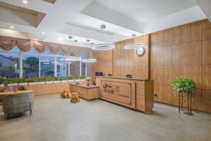Uma área de recepção com balcão de madeira, espaço de estar com sofá e uma janela grande com cortinas.