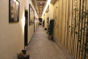 Um corredor com quadros nas paredes, plantas em vasos e uma cerca de bambu.