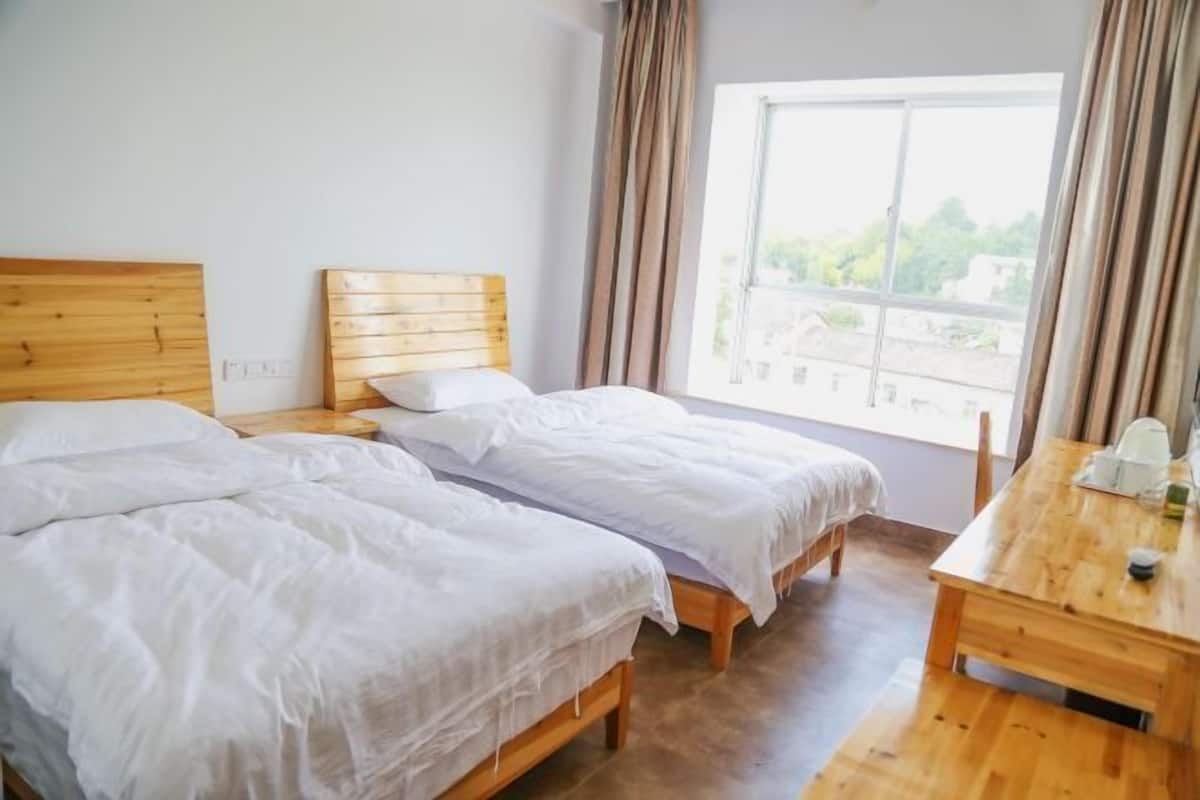 Quarto com duas camas de madeira, uma mesa de madeira e uma janela com cortinas.