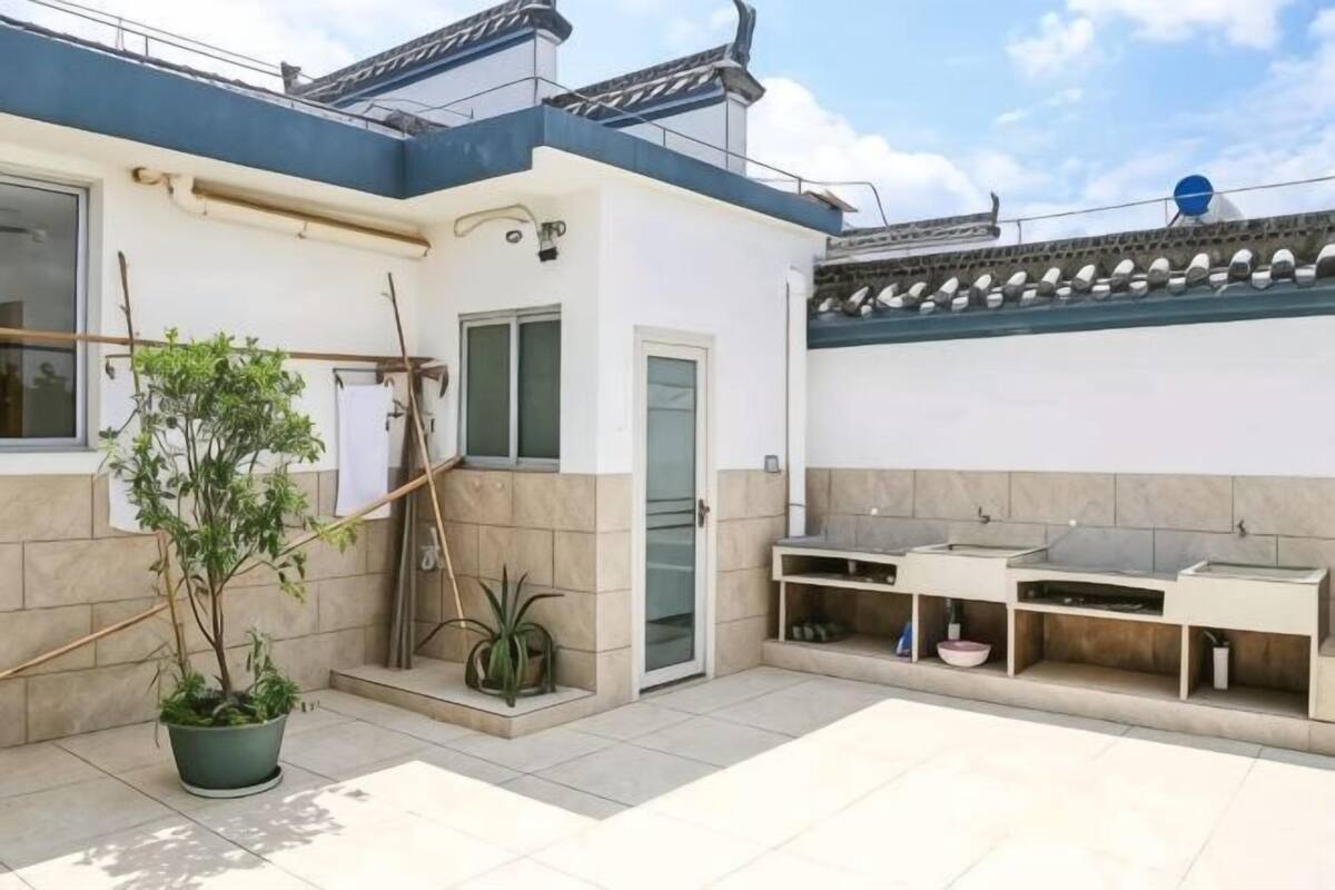 Um edifício residencial com pátio ladrilhado, porta, pequeno jardim com plantas em vasos e telhado tradicional.