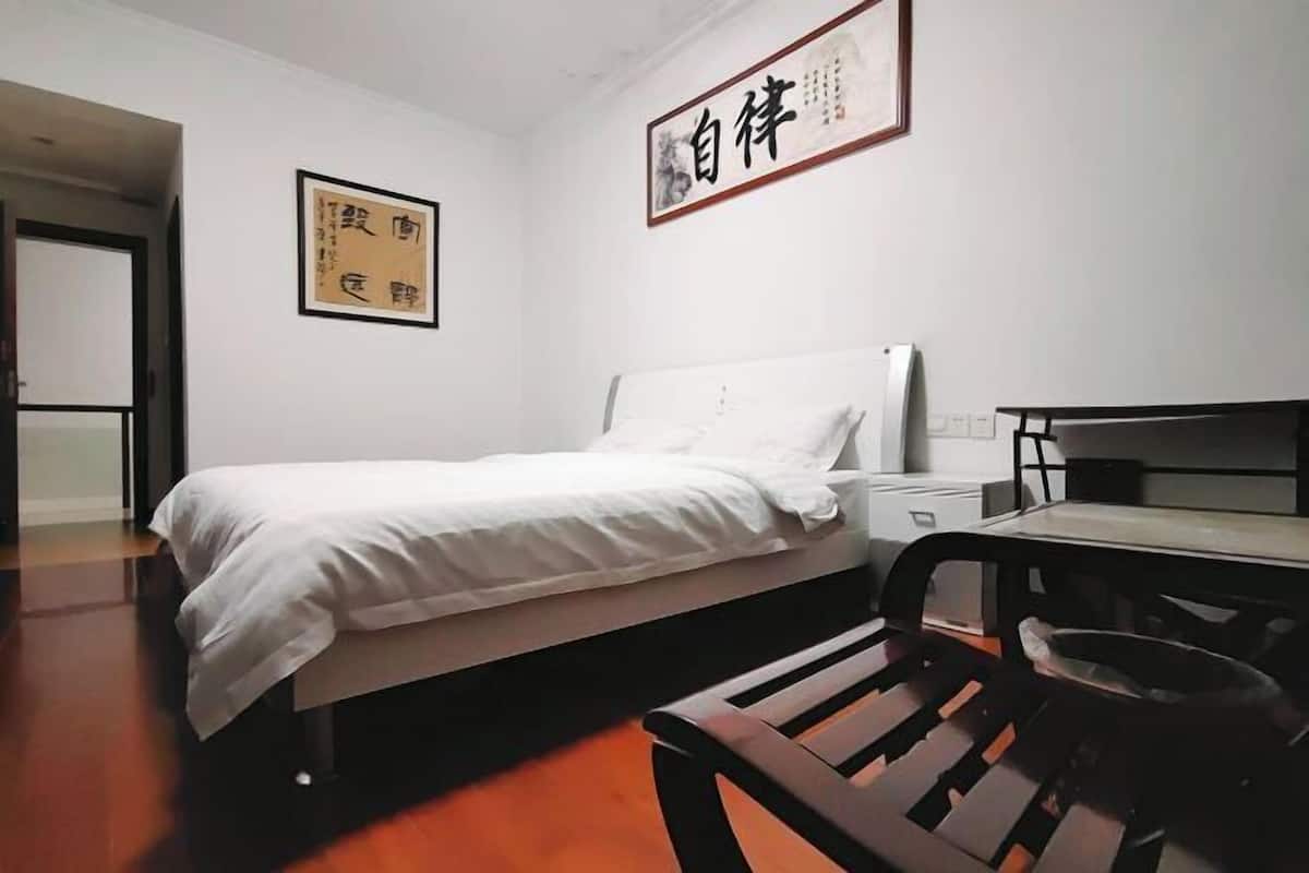 Quarto com cama, escrivaninha e cadeira. Há dois objetos emoldurados na parede.