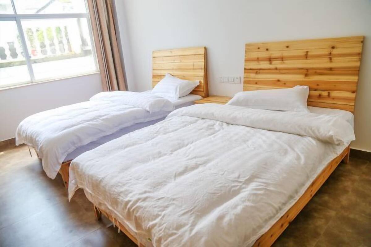 Quarto com duas camas, cabeceiras de madeira, roupa de cama branca e uma janela com cortinas.