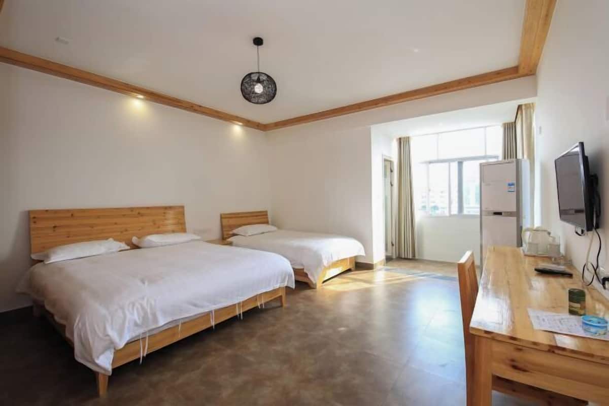 Quarto de hotel com duas camas de solteiro, uma secretária de madeira com televisão e uma janela grande que proporciona iluminação natural.