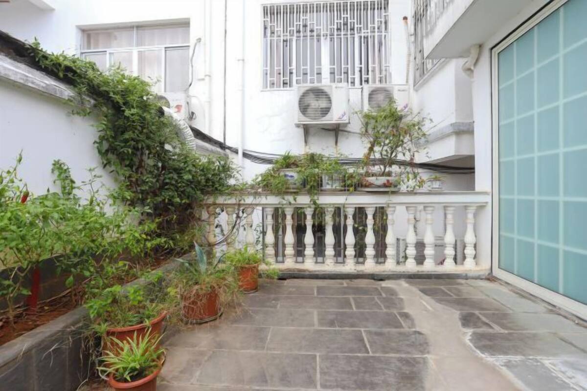Um pátio com plantas em vasos, chão de pedra e um edifício branco com janelas com grades e aparelhos de ar condicionado.