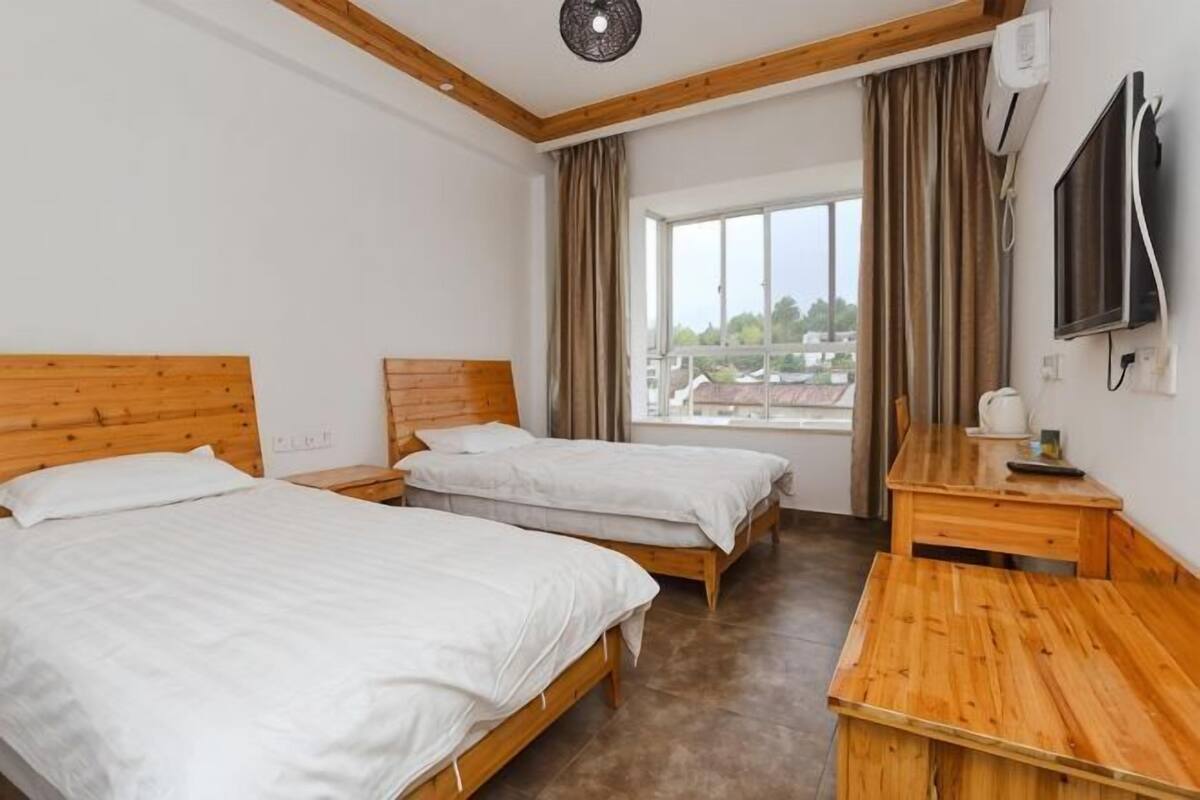 Quarto de hotel com duas camas, uma escrivaninha de madeira, televisão e janela com cortinas.