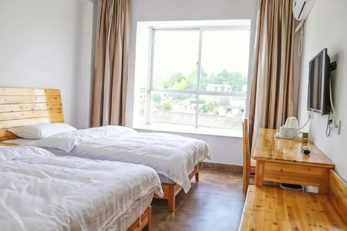 Quarto com duas camas, uma mesa de madeira, televisão e janela com cortinas.