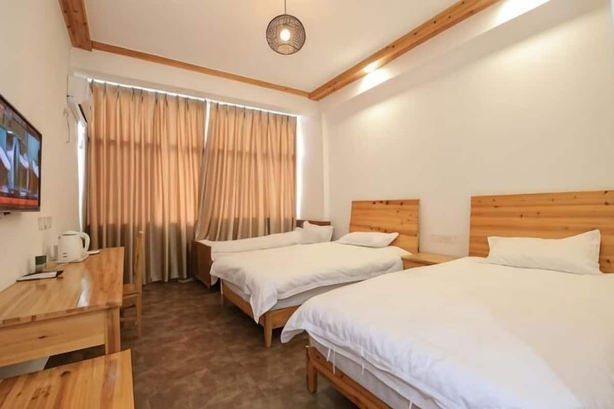 Quarto de hotel com duas camas, uma escrivaninha, televisão e janela com cortinas.