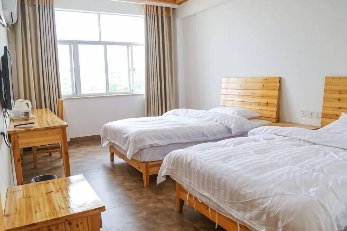 Quarto com duas camas de madeira, uma escrivaninha de madeira, uma cadeira, televisão e janela com cortinas.