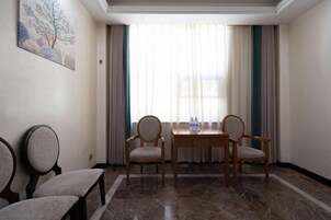 Quarto com piso de mármore, duas cadeiras de madeira, uma mesa pequena e um quadro na parede.