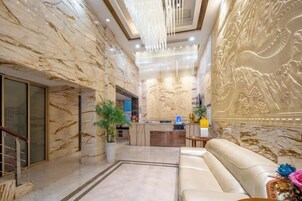 Um hall de hotel com paredes de mármore, um balcão de recepção, um sofá e um lustre.