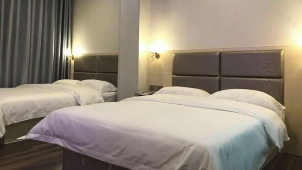 Quarto de hotel com duas camas, uma janela grande com cortinas e um aplique na parede.