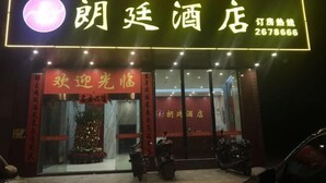 Entrada de hotel com letreiro de neon, árvore de Natal e scooters estacionadas na frente.