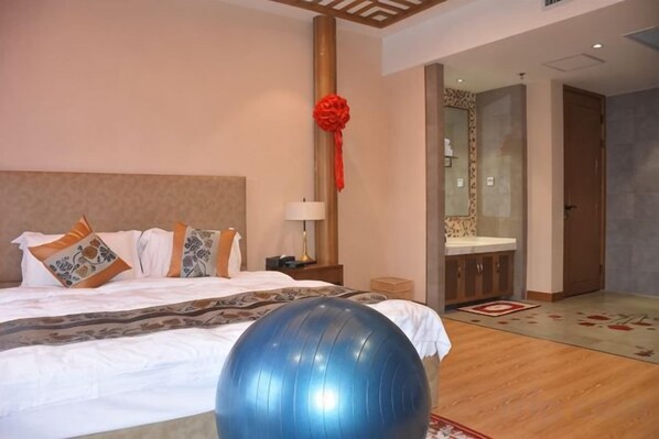 Quarto de hotel com uma cama grande, uma mesa de cabeceira, um espelho e um objeto decorativo vermelho na parede.