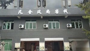 Um edifício com uma placa que diz "Feng Chuang Hotel". Há unidades de ar condicionado nas paredes externas e duas portas abertas no nível da rua.