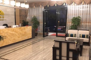 Recepção de hotel com balcão de mármore, assentos e entrada por porta de vidro.